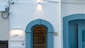 Entrada de um edifício com um arco azul, uma placa com o texto "B-WELCOME" e o número "27" na parede.