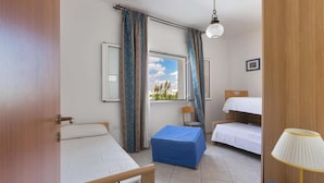 Um quarto com duas camas, uma janela com cortinas, uma luminária e uma cadeira.