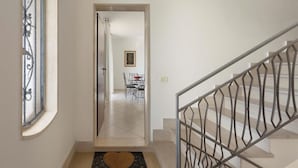 Uma escadaria com corrimão geométrico leva a uma área de refeições com mesa e cadeiras.