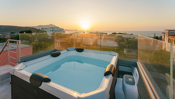 Uma banheira de hidromassagem no terraço com vista para o pôr do sol sobre o mar.