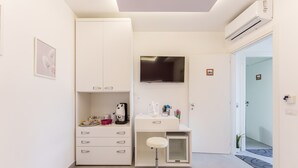 Um banheiro moderno e minimalista, com toucador branco, televisão montada e uma pequena área de estar.