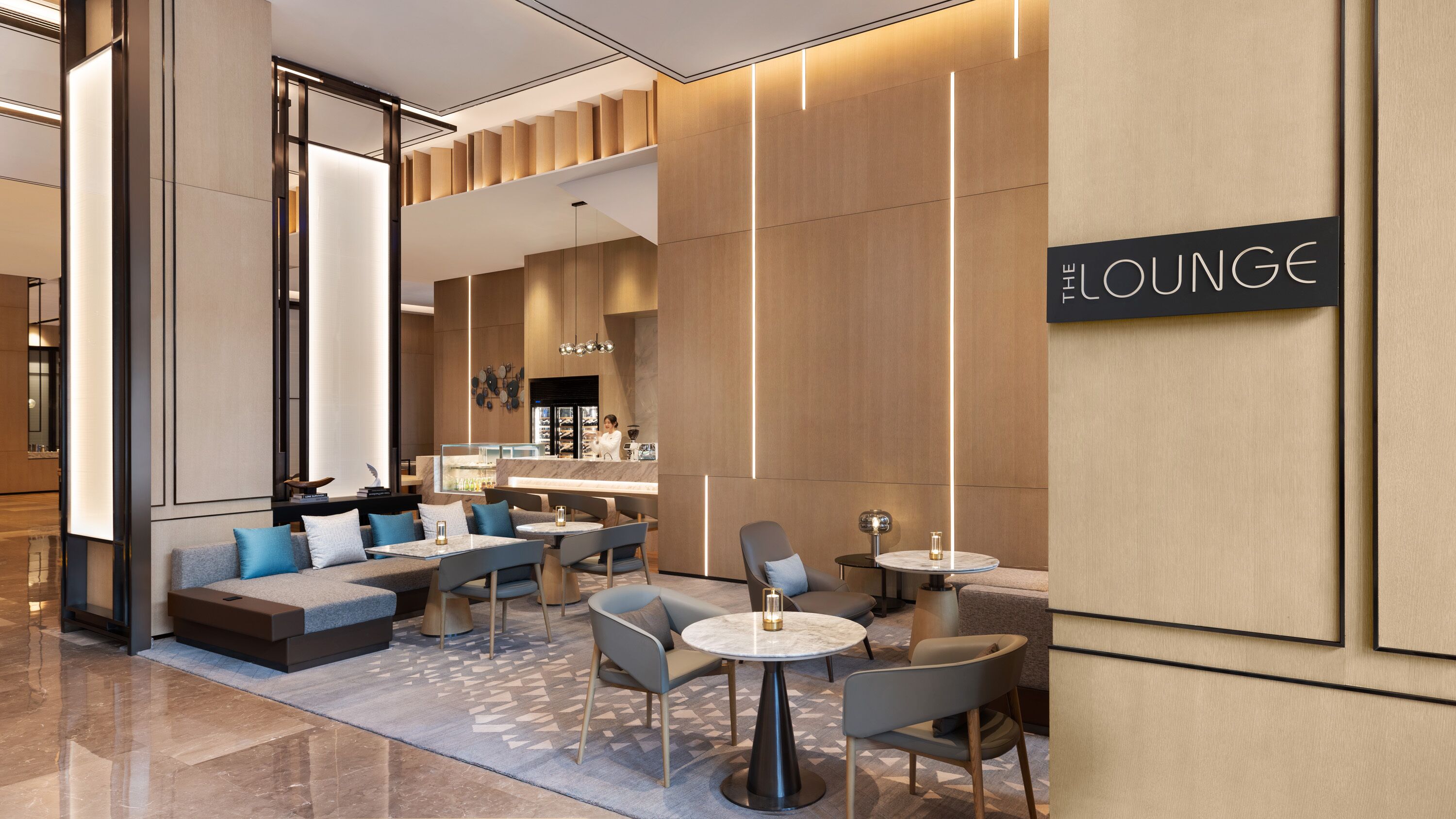 Uma área de estar moderna com sofás, um bar e uma placa com a inscrição 'THE LOUNGE'.