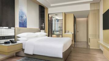 Quarto de hotel moderno com cama, mesa de cabeceira e banheiro visível por uma porta aberta.
