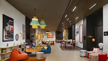 Um interior moderno com área de estar central, várias mesas e uma variedade de cadeiras e pufes coloridos.
