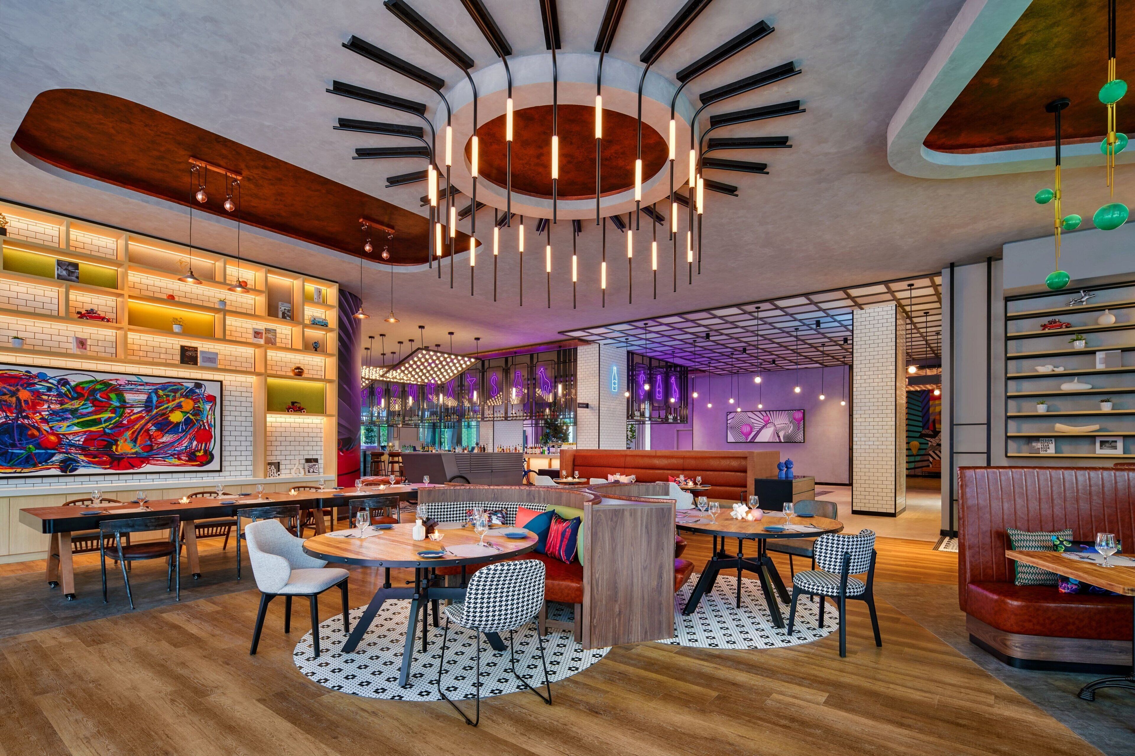 Um restaurante moderno com mesas de madeira, obras de arte coloridas e um design de teto singular.