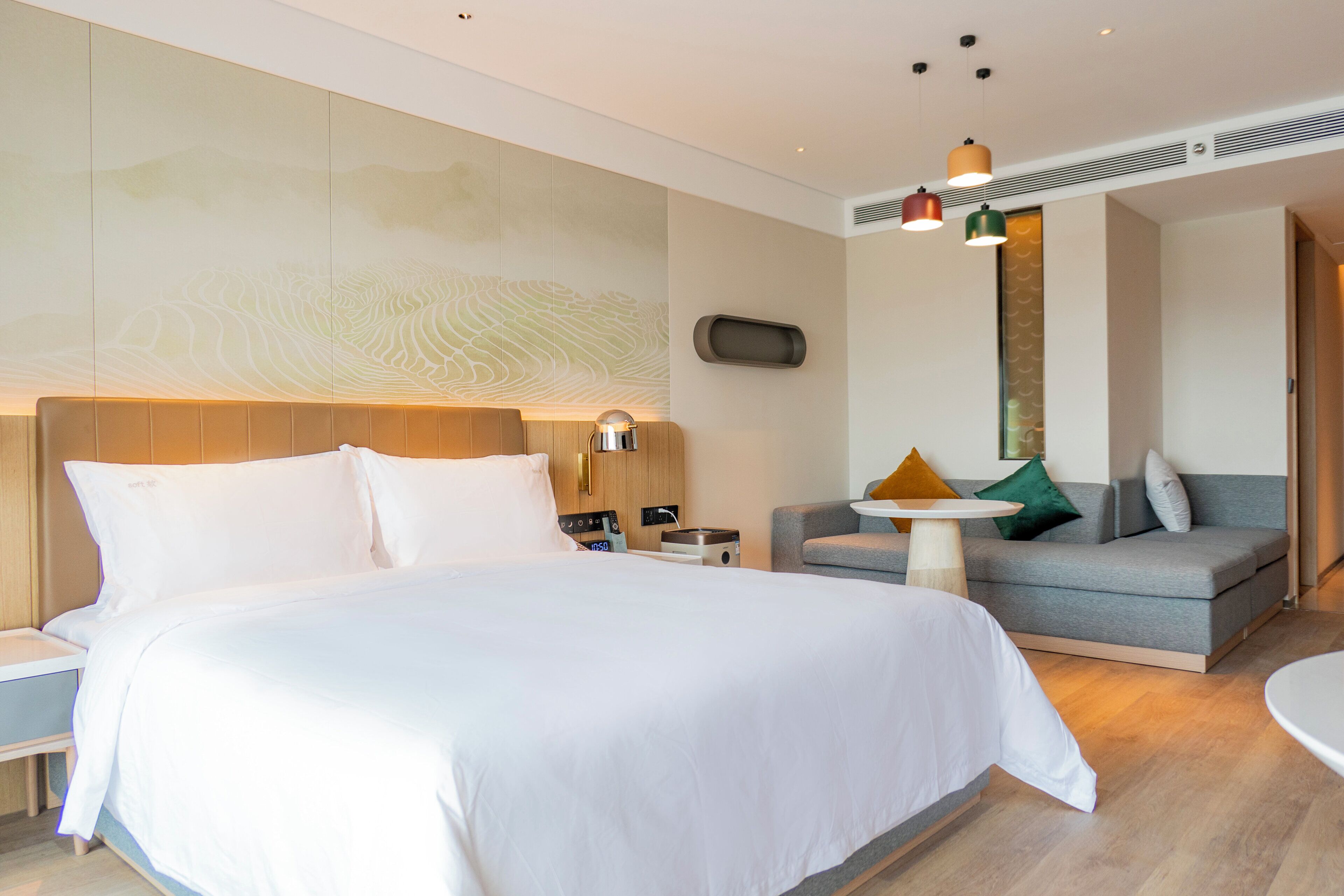 Quarto de hotel com uma cama grande, um sofá, uma mesinha e uma TV fixada na parede.
