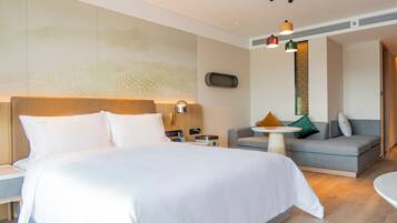 Quarto de hotel com uma cama grande, um sofá, uma mesinha e uma TV fixada na parede.