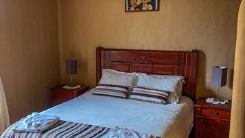 Uma cama bem arrumada com roupa de cama listrada, duas mesas de cabeceira com abajures, uma cabeceira de madeira e um quadro na parede.