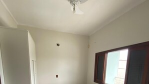 Quarto com uma cama, ventilador de teto, janela com persianas e porta.