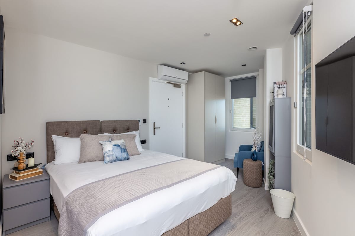 Quarto moderno com cama grande, mesas de cabeceira, guarda-roupa e janela com vista.