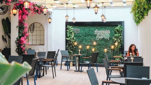 Interior de restaurante com mesas e cadeiras, luminárias pendentes e uma parede verde com o logotipo em formato de coração.