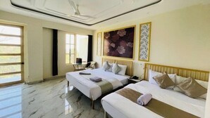 Quarto de hotel com duas camas, ventoinha no teto, uma janela grande e um quadro na parede.