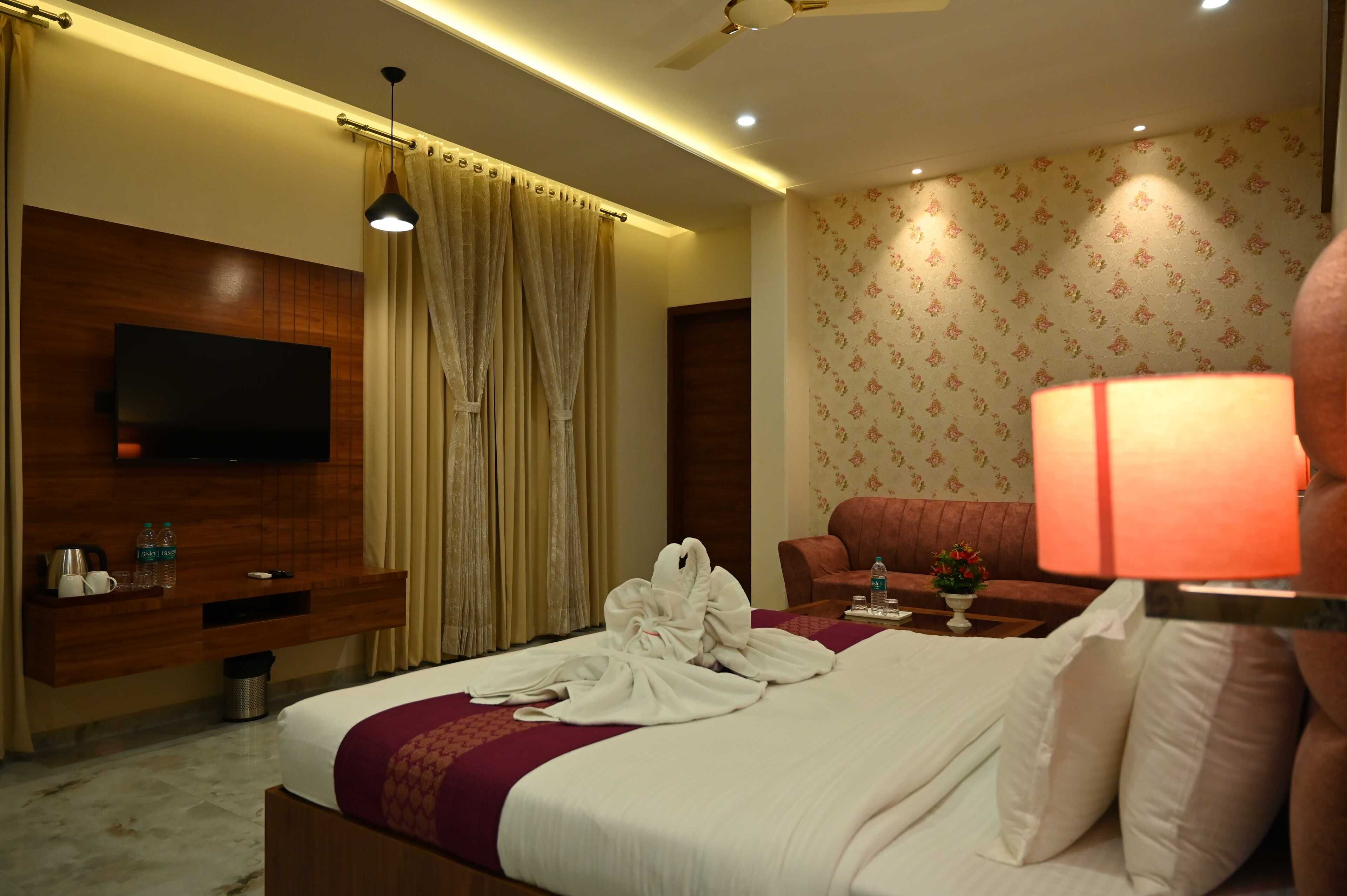 Quarto de hotel com cama, televisão, escrivaninha com luminária, cadeira e parede com papel de parede floral.