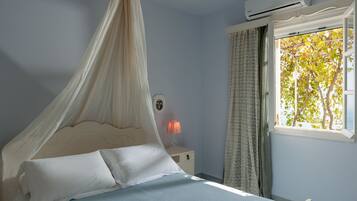 Quarto com cama de dossel, luminária de cabeceira e janela com vista para árvores.