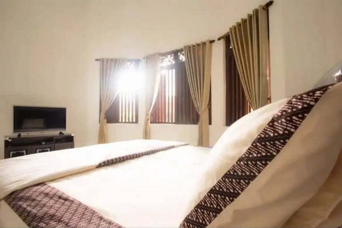 Quarto de hotel com uma cama, uma televisão sobre um suporte e cortinas nas janelas.
