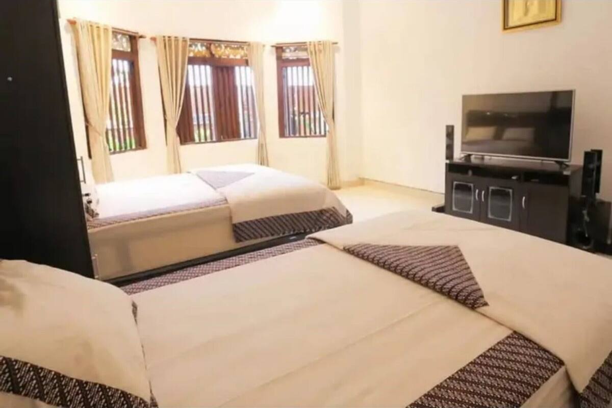 Quarto de hotel com duas camas, televisão sobre um móvel e janelas com cortinas.