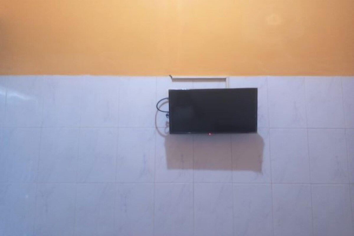 Quarto com parede de azulejos brancos e uma televisão de ecrã plano preta fixada na parede.