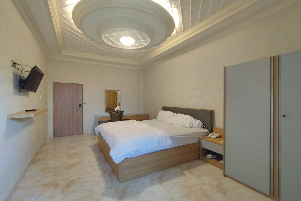 Quarto com cama, mesa de cabeceira, guarda-roupa e televisão na parede.