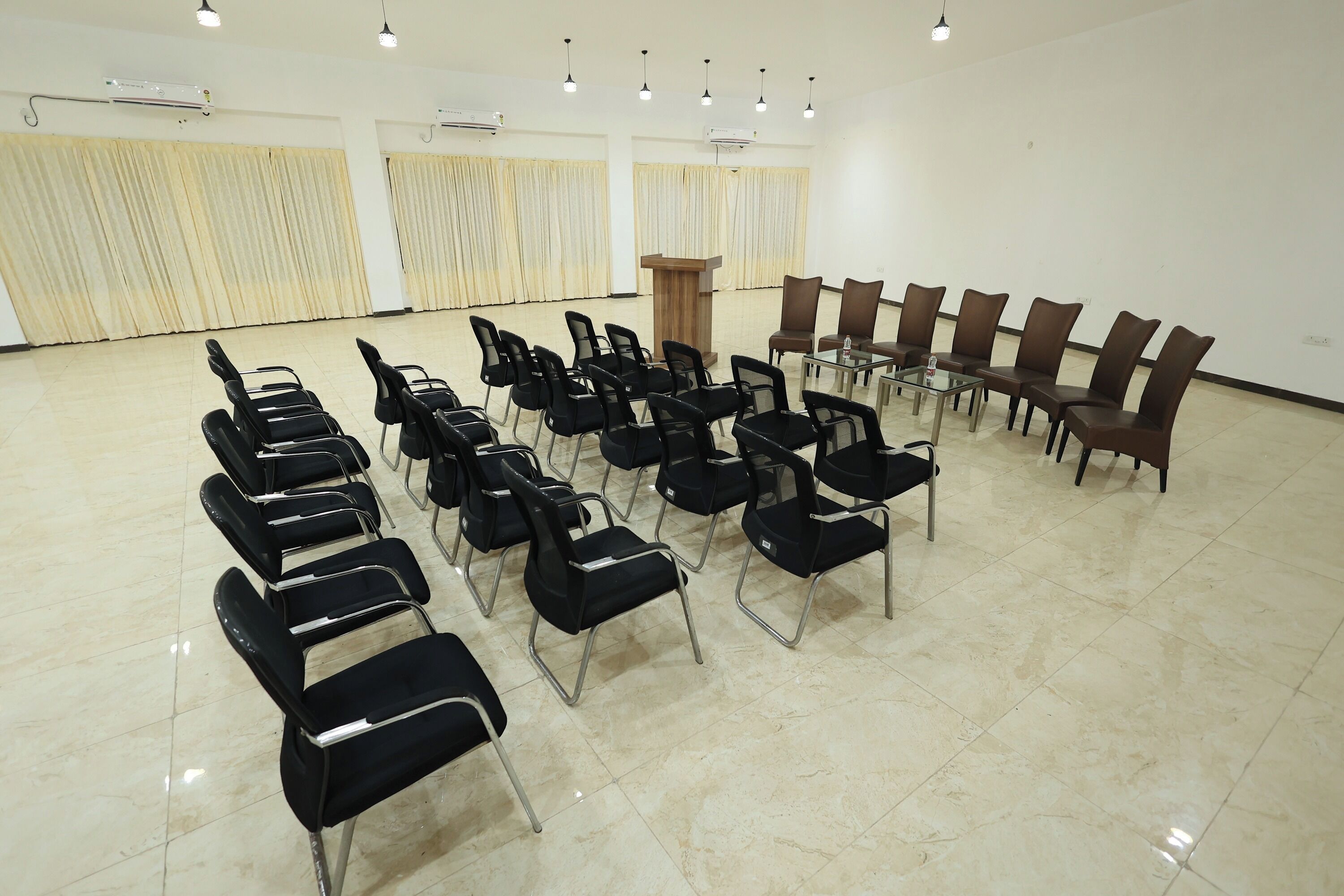 Uma sala de conferências com fileiras de cadeiras, um púlpito e uma mesa de vidro.