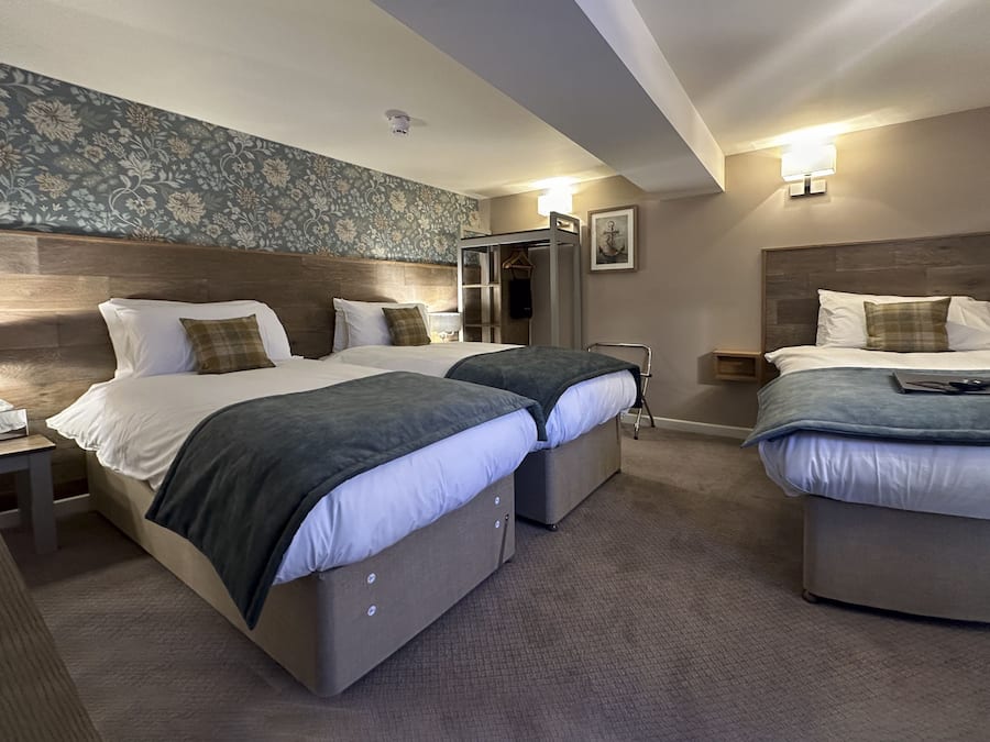 Quarto de hotel com duas camas, um guarda-roupa, uma mesa de cabeceira e um espelho.