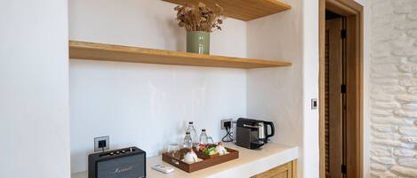 Uma cozinha com cafeteira, rádio e um vaso com flores secas numa prateleira.