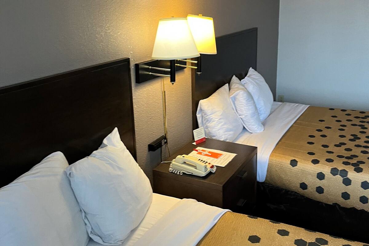 Quarto de hotel com duas camas, uma mesinha de cabeceira com abajur e uma placa na parede.