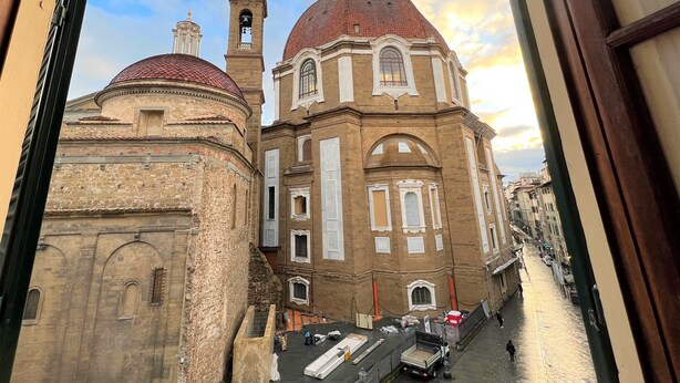 Um edifício histórico com uma torre de sino e uma cúpula, visto de uma janela.