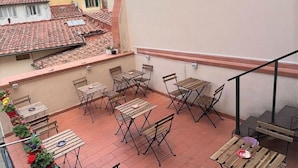 Um terraço no telhado com mesas e cadeiras de madeira, rodeado por vasos de plantas.