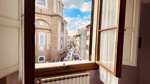 Quarto com janela para uma rua com edifícios históricos.