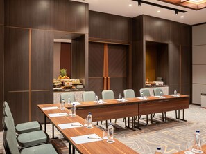 Uma sala de conferência com uma mesa comprida, cadeiras, garrafas de água e uma seleção de frutas.