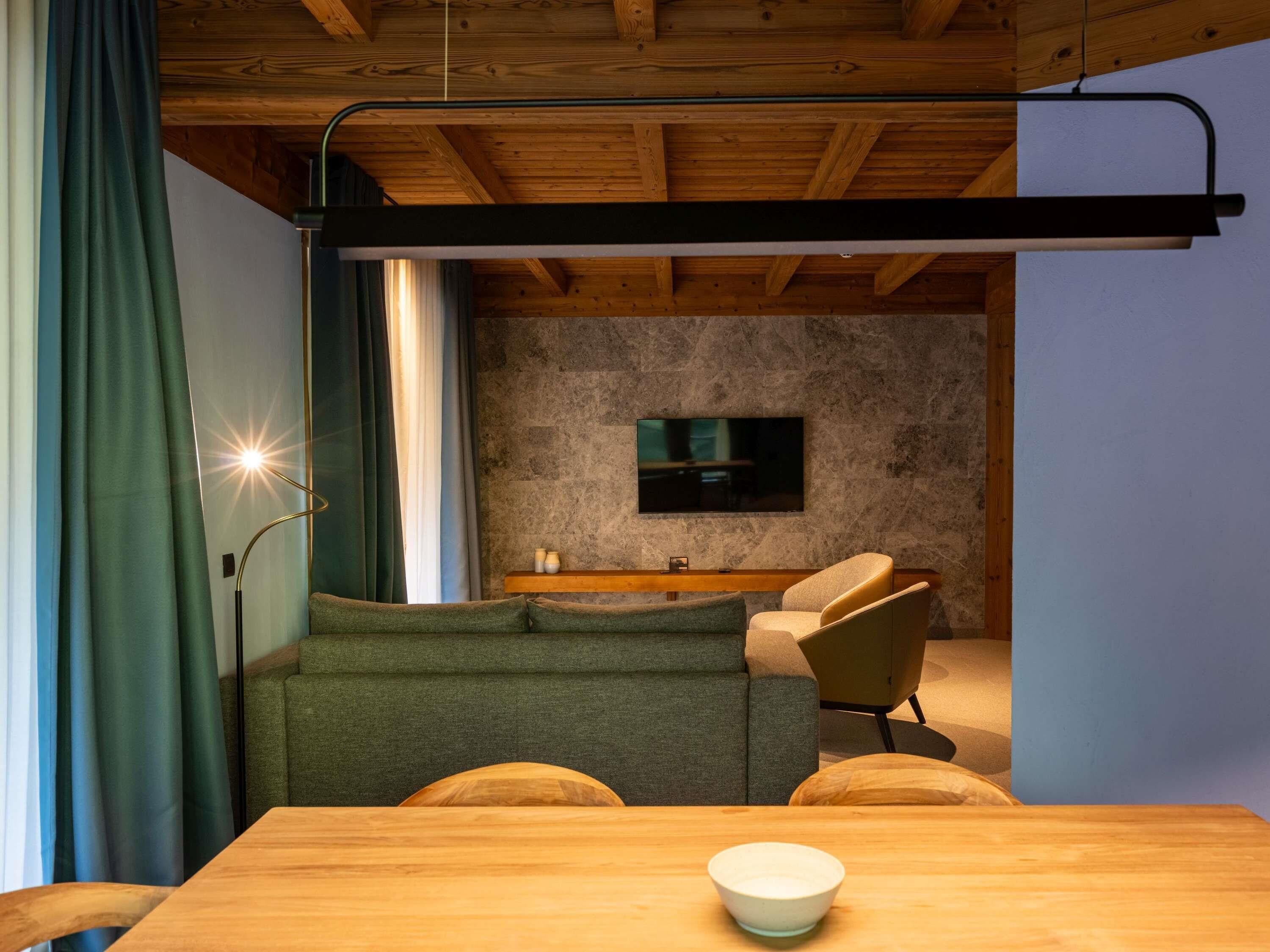 Um quarto acolhedor com teto de madeira, um sofá, uma mesa de jantar e uma televisão fixada em uma parede com textura.