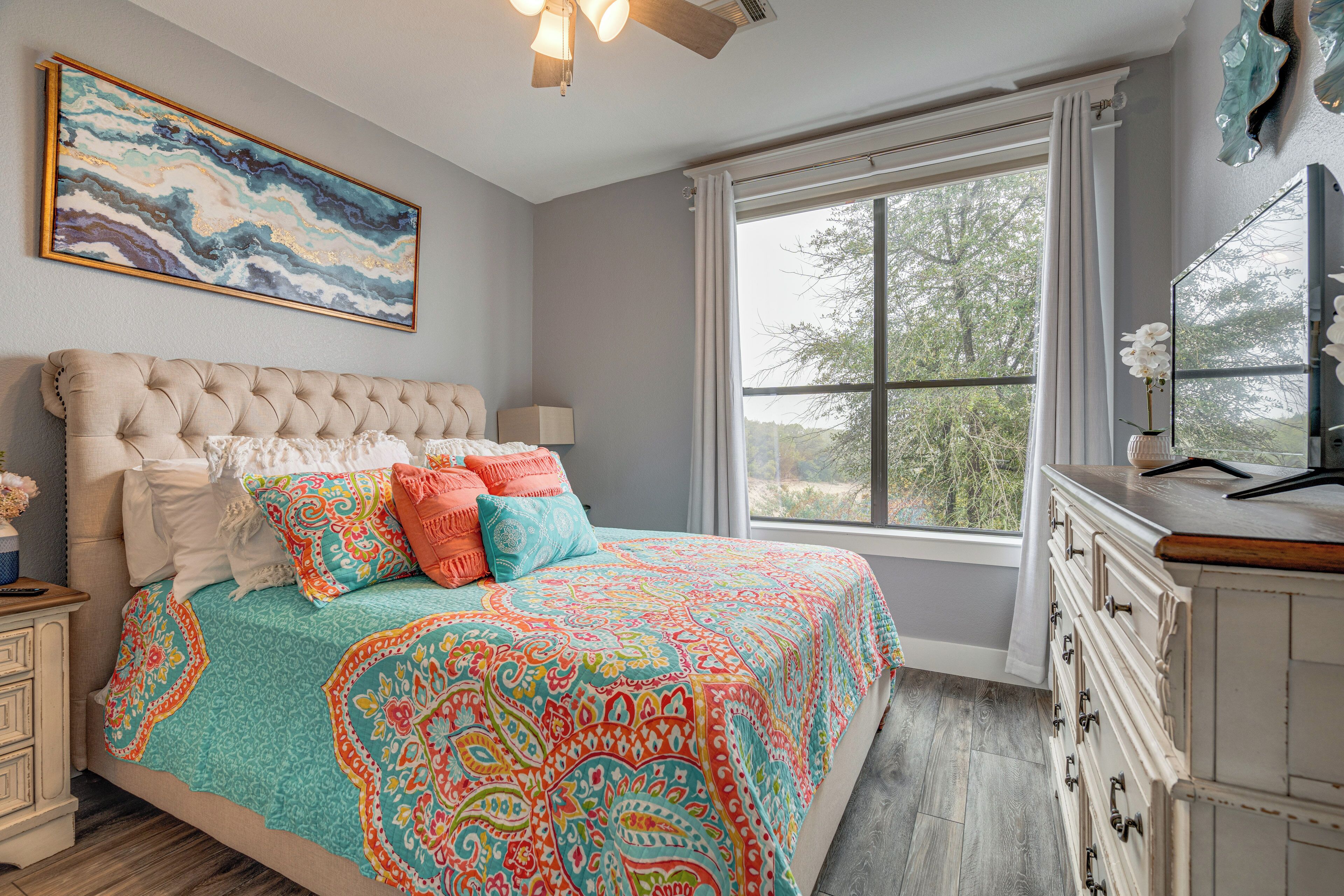 Quarto com uma cama grande, cômoda, janela com cortinas e um quadro na parede.