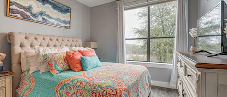 Quarto com uma cama grande, cômoda, janela com cortinas e um quadro na parede.