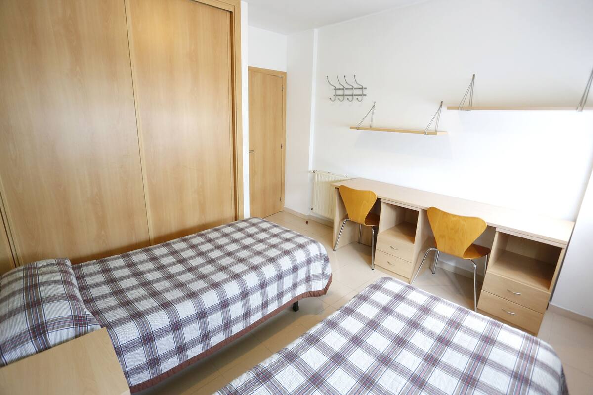 Quarto com duas camas, uma escrivaninha e uma cadeira.