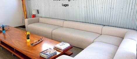 Uma sala de estar moderna com uma mesa de centro de madeira, sofá bege e parede listrada com o texto "micampus Lugo".