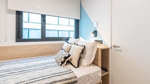 Quarto com uma cama, mesa de cabeceira, abajur e janela com persianas.