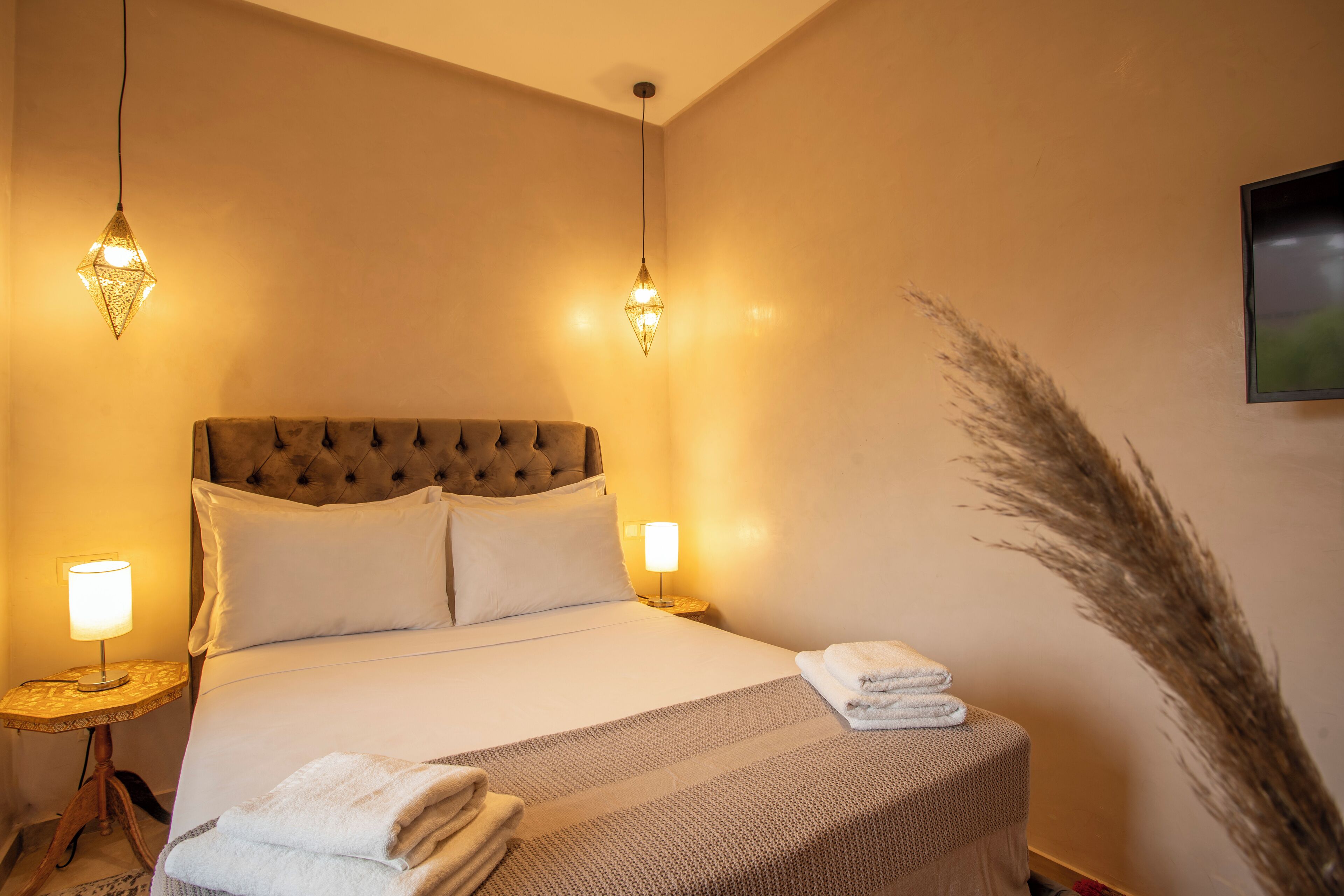 Cama bem arrumada com cabeceira estofada, duas luminárias de cabeceira e um quadro na parede.