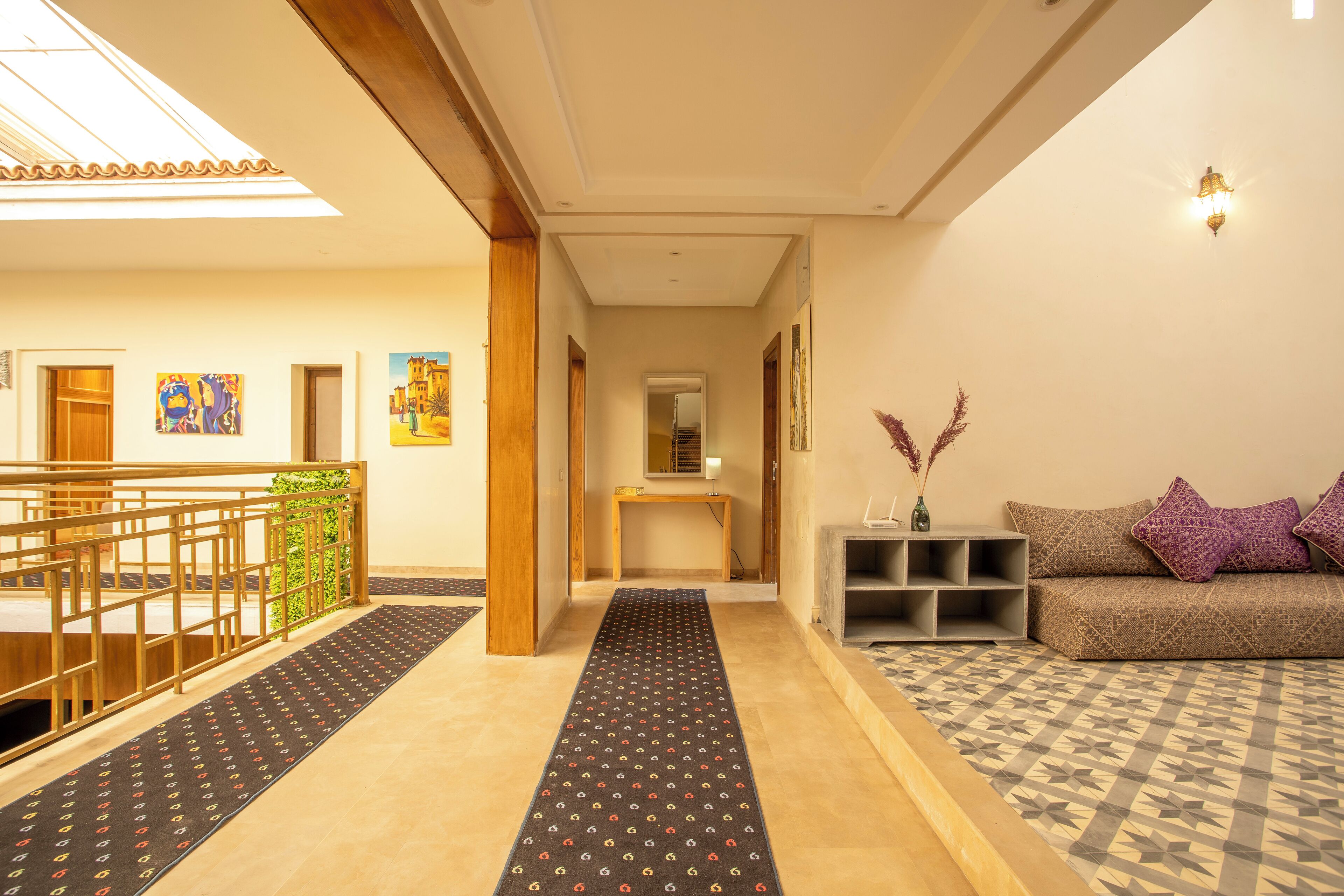 Um saguão de hotel com escadas de madeira, balcão de recepção, sofá com almofadas e obras de arte nas paredes.