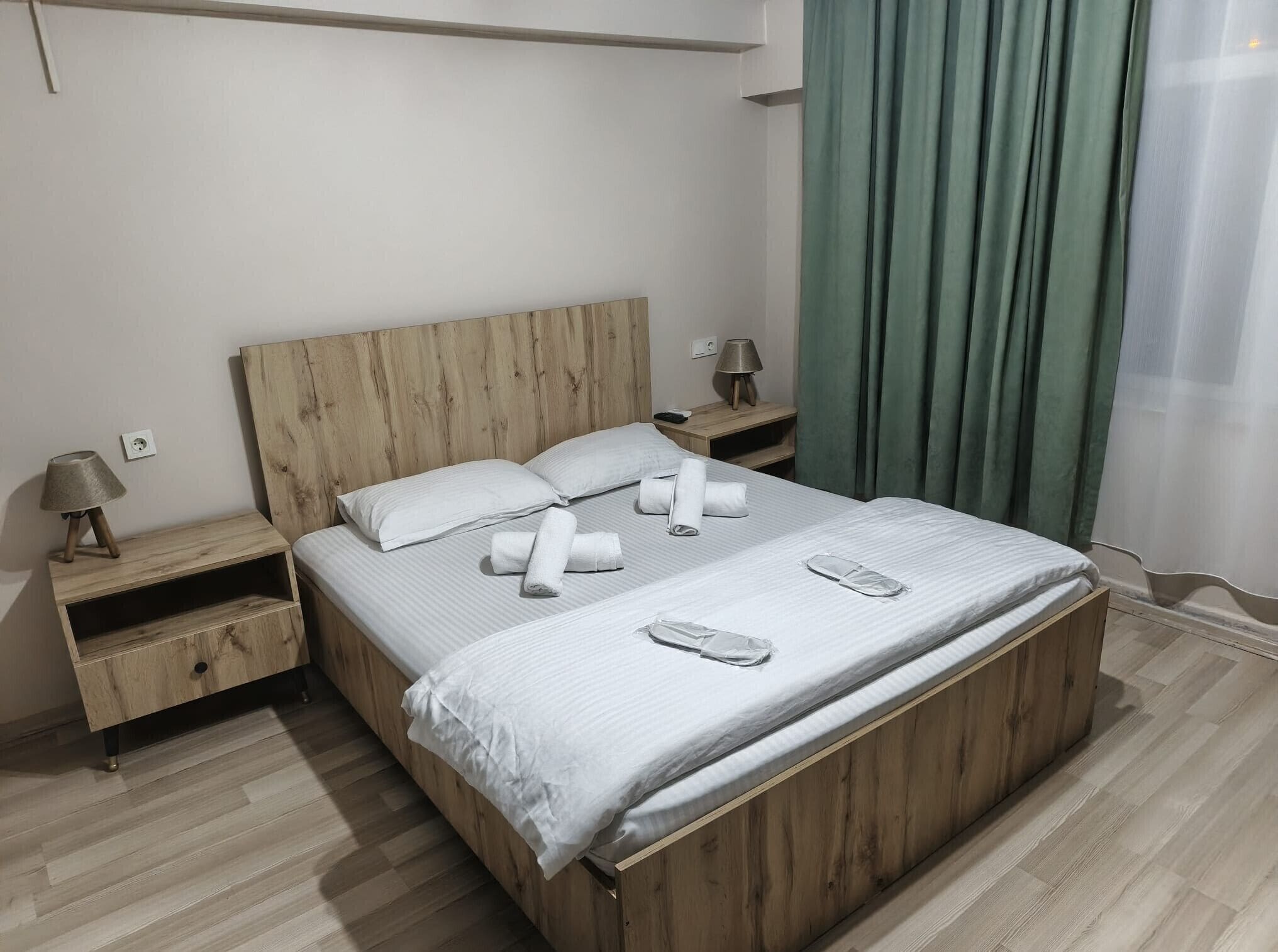 Uma cama de casal bem arrumada, com cabeceira de madeira, mesa de cabeceira com abajur e criado-mudo com controle remoto.