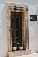 Janela com grades de metal, um vaso de planta e um aviso com a inscrição 'Casa Hotel Boutique Madero 99'.
