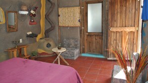 Um quarto rústico com uma cama, uma mesinha, um espelho e uma porta de madeira.