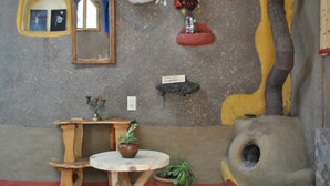 Um interior rústico com uma mesa de madeira, plantas em vasos, um espelho e uma pequena prateleira com uma placa de identificação.