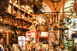 Uma loja de antiguidades cheia de objetos diversos à mostra, incluindo um sino, uma estátua e uma máquina de refrigerantes Coca-Cola.