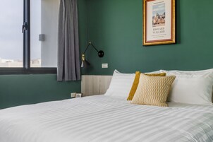 Uma cama bem arrumada com roupa de cama listrada, um quadro na parede, um abajur e uma janela com cortinas.