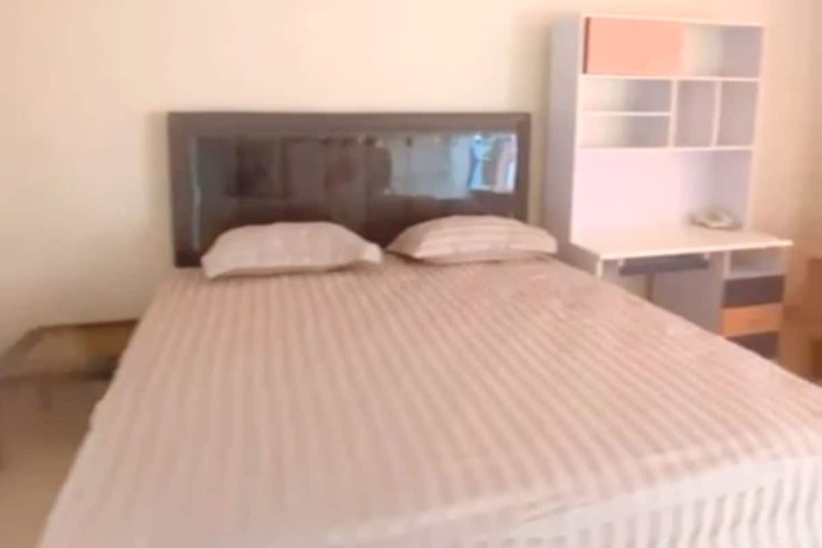 Quarto com cama, cabeceira e secretária embutida com espaço de armazenamento.