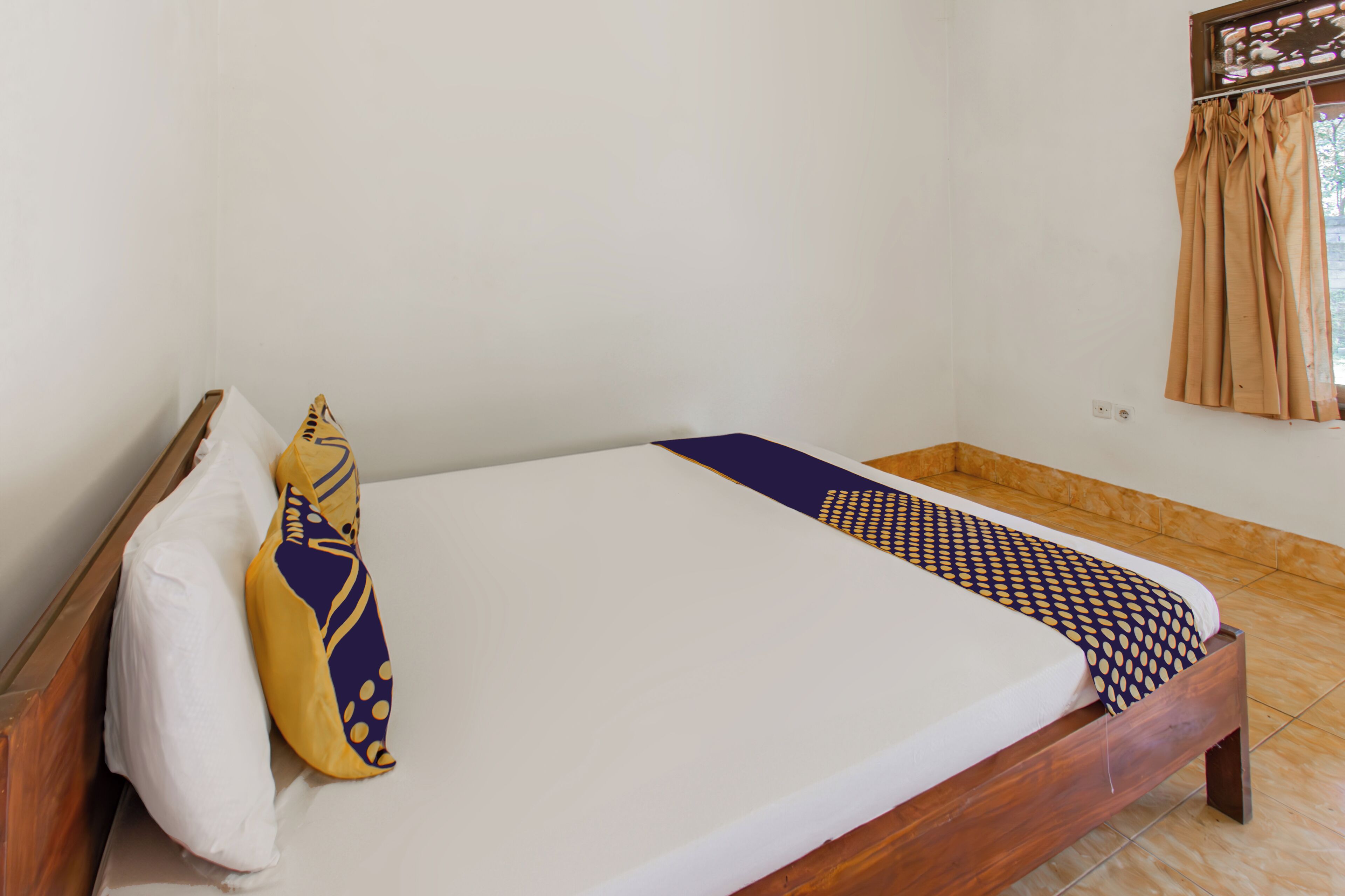 Uma cama de solteiro com estrutura de madeira, roupa de cama branca e um cobertor estampado.