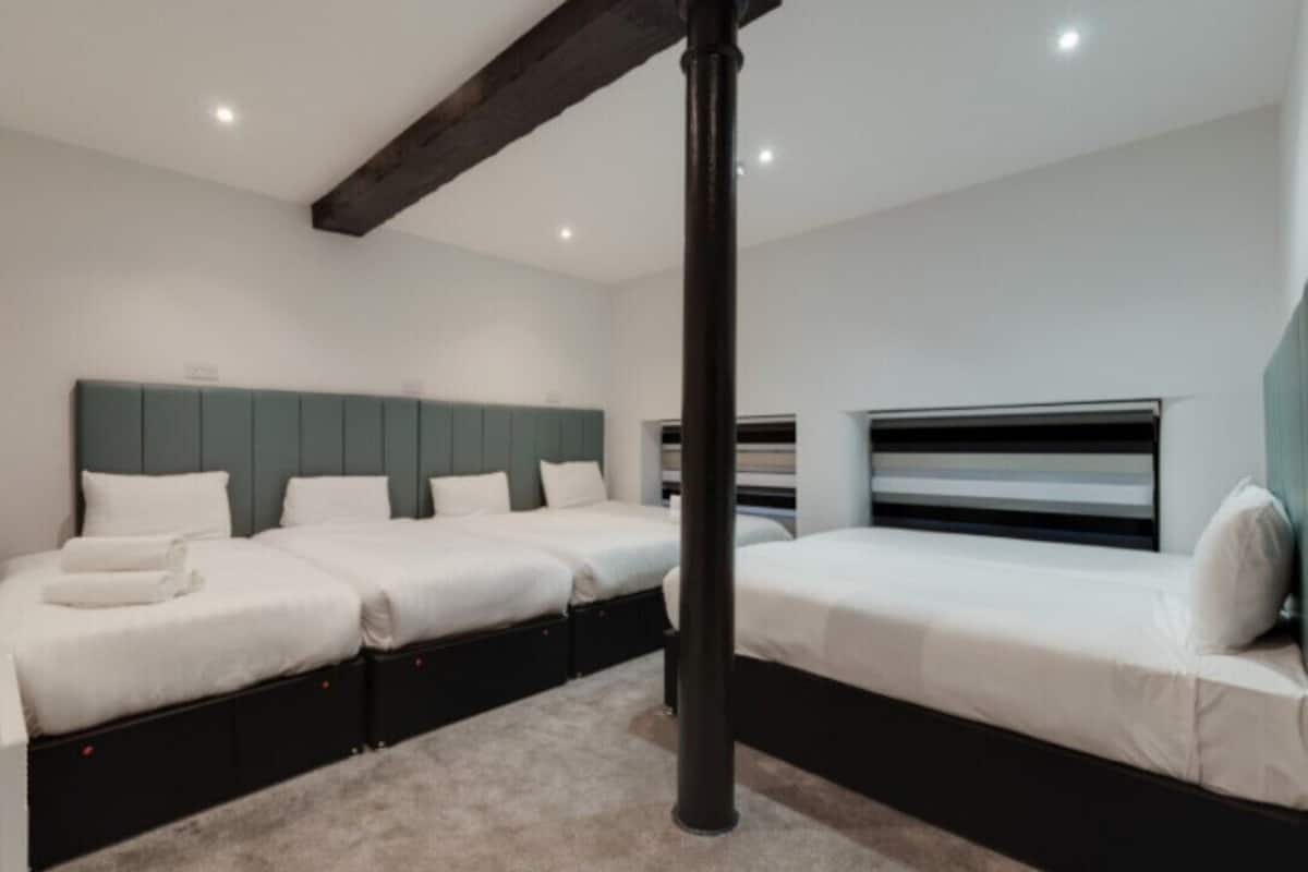 Quarto de hotel com três camas, um pilar escuro e teto branco.