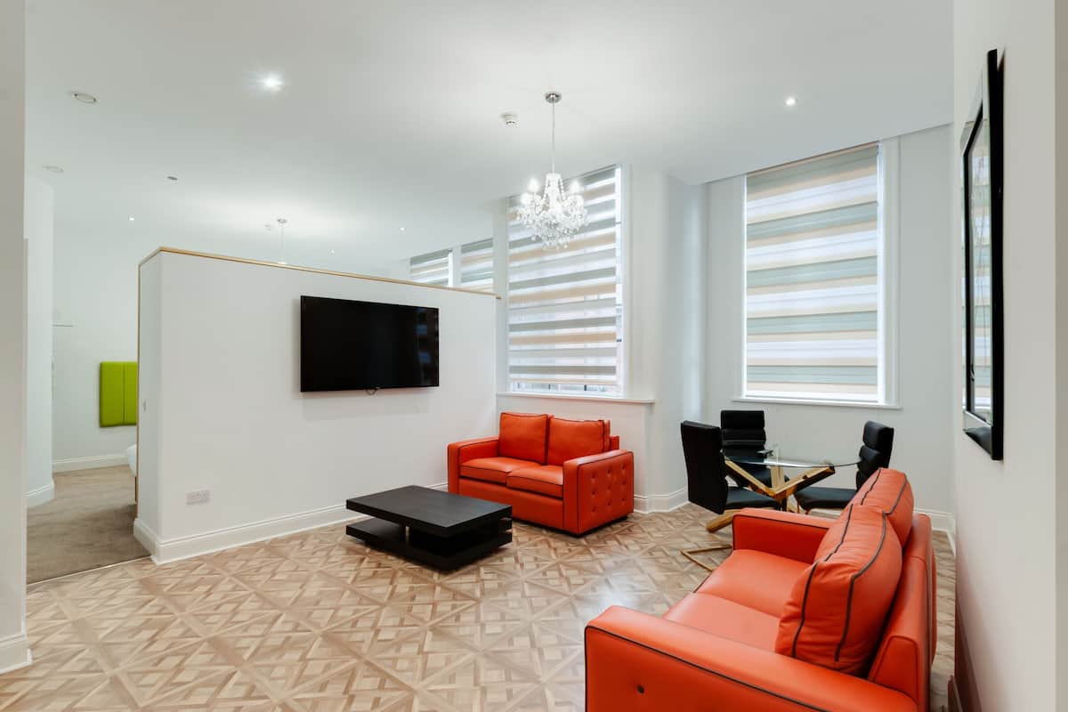 Uma sala de estar moderna com uma televisão de tela plana grande, sofás laranja, uma mesa de centro e um candelabro.