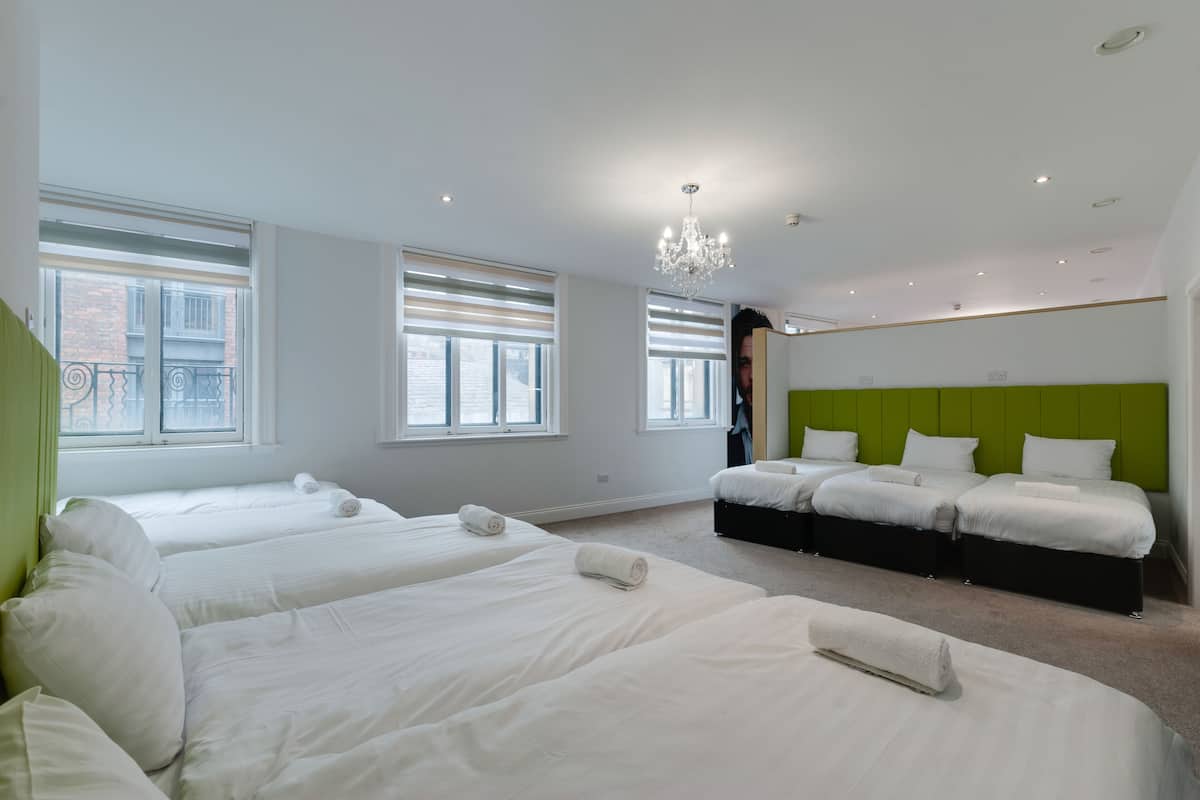 Quarto de hotel com duas camas de solteiro, uma cama maior e uma parede verde de destaque.