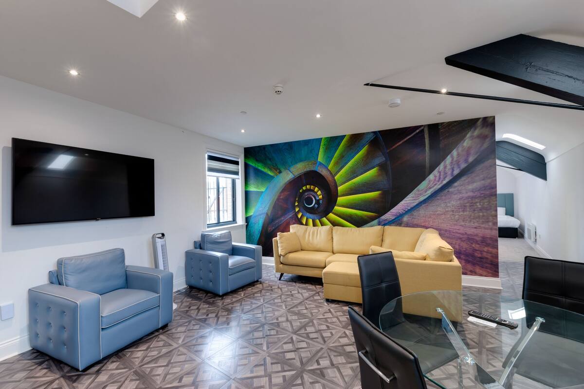 Uma sala de estar moderna com uma grande TV de tela plana, dois sofás, uma mesa de centro de vidro e um mural vibrante na parede.
